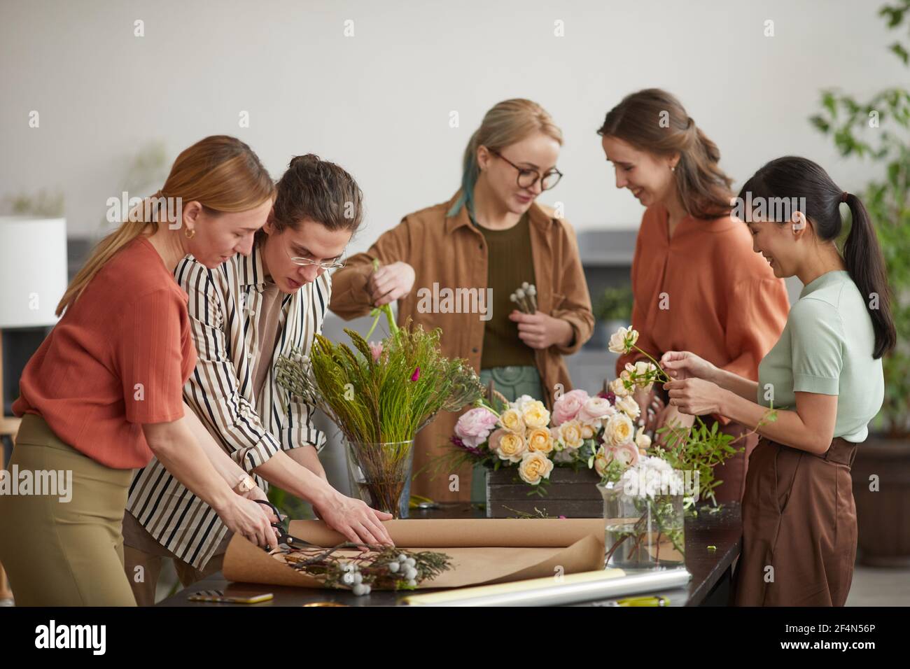 Diverse group of young florists arranging floral compositions while ...