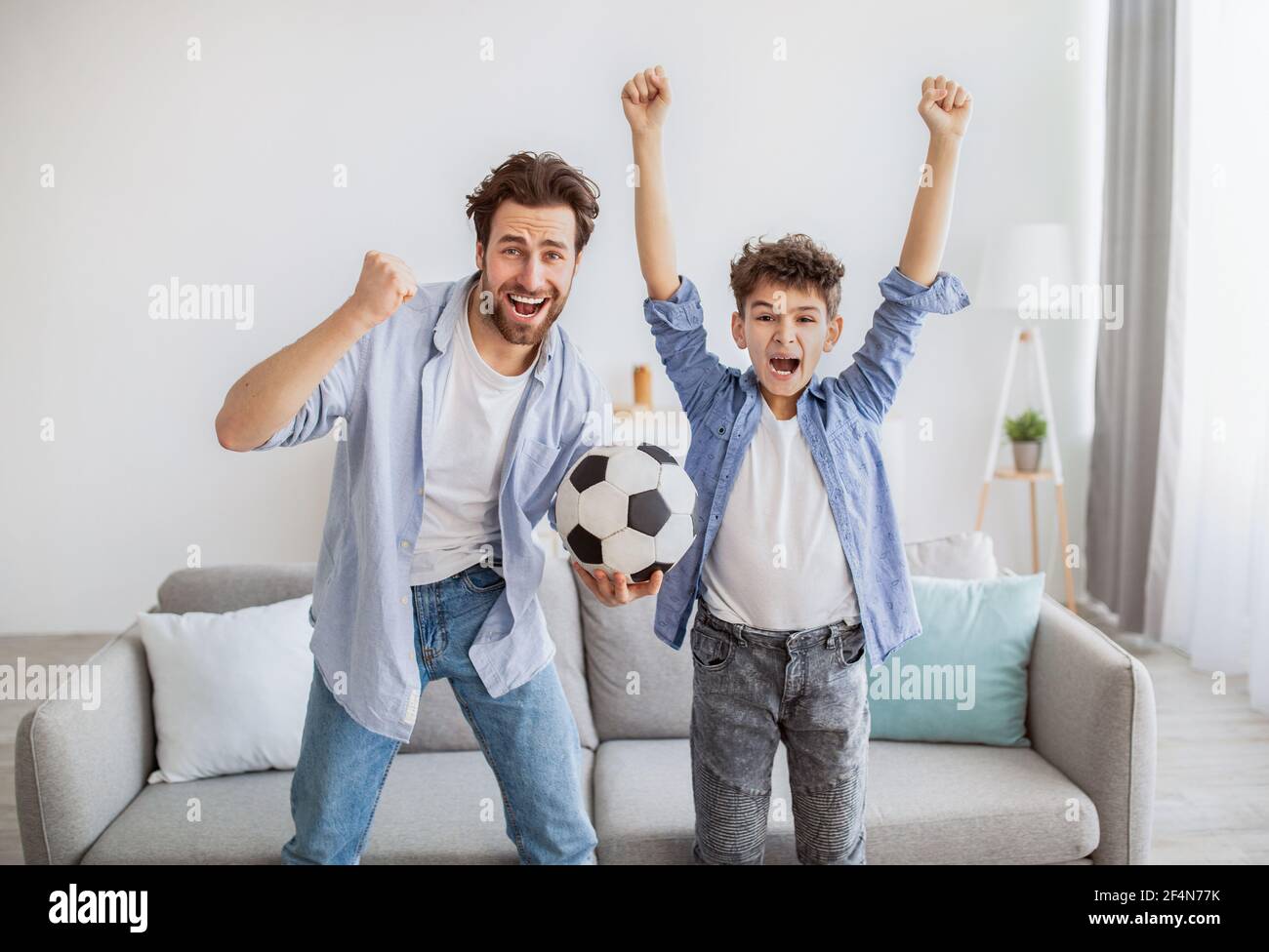 Emotional soccer fans. Cheerful dad and son cheering with football ball ...