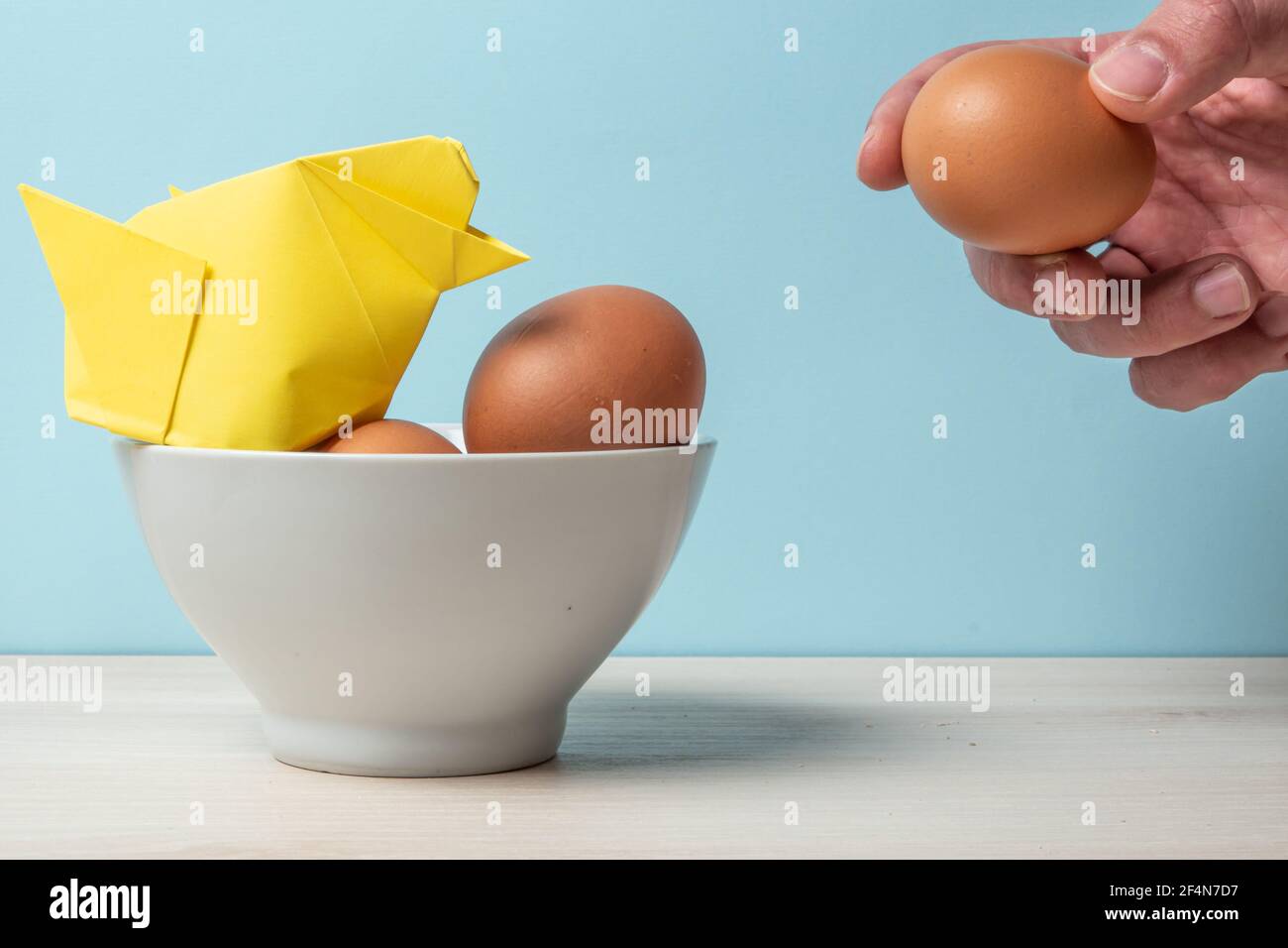 Hen origami looking at hand getting an organic egg against blue ...