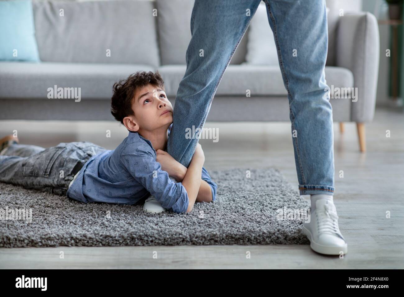 Please stay, dad. Sad little boy embracing his father leg and looking ...