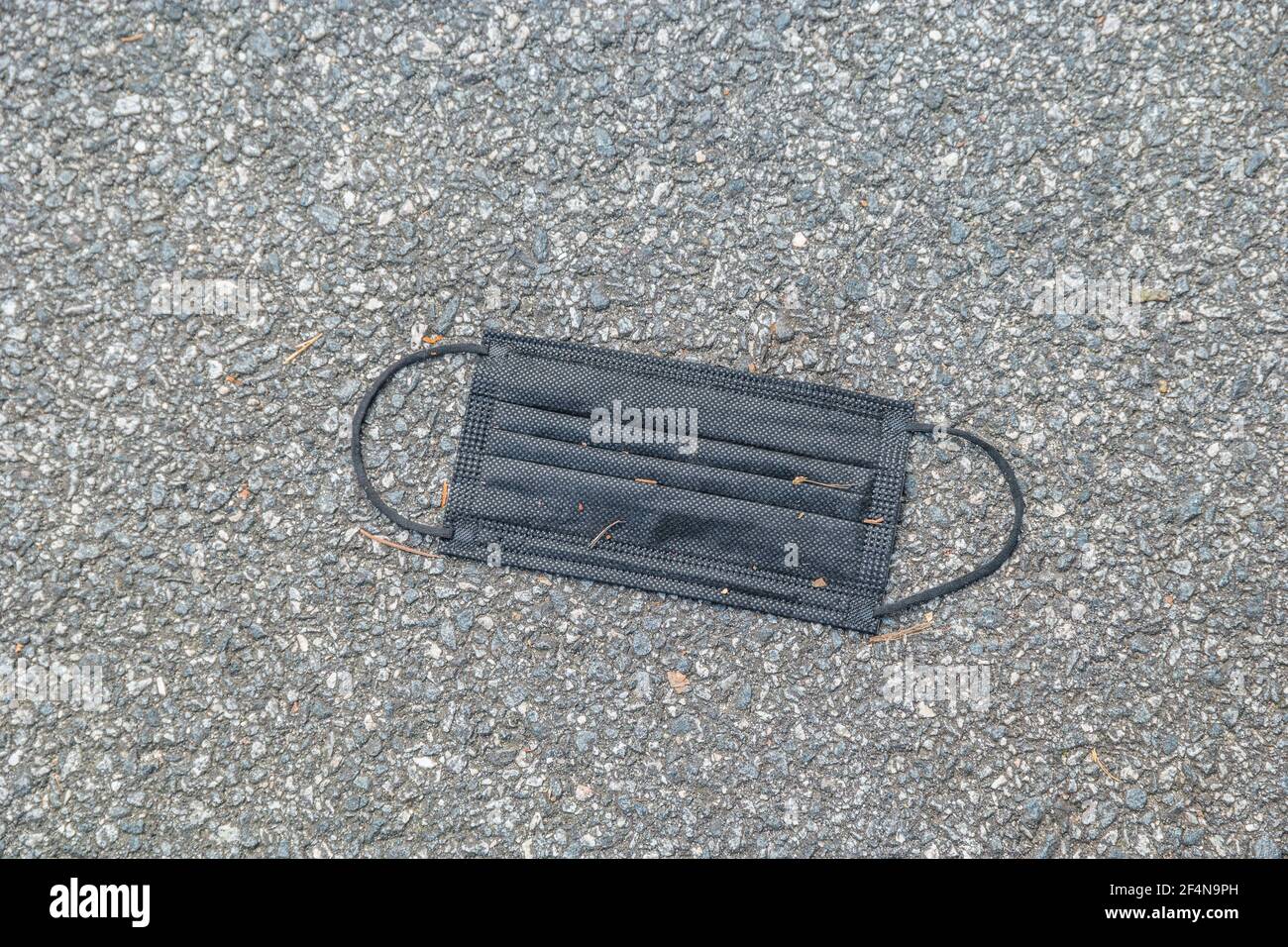 A black dirty face mask laying on the ground discarded improperly ...