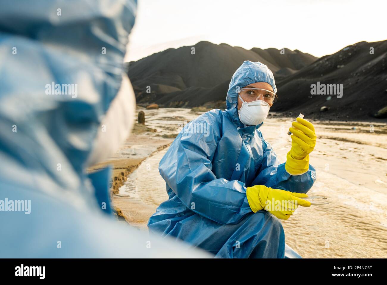 One of two young female ecologists in rubber gloves, protective ...