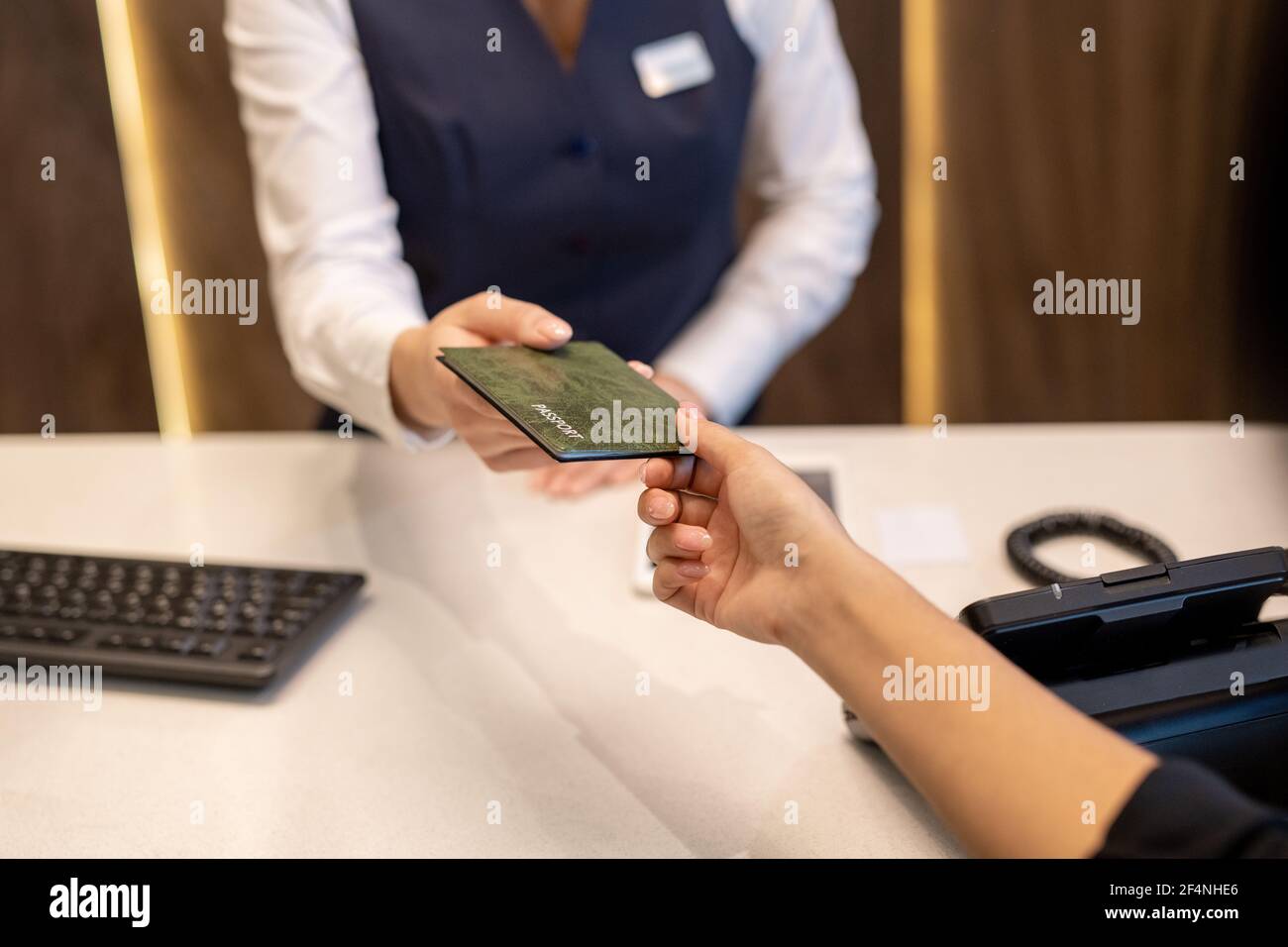 Hand of young female receptionist passing passport to one of new guests ...