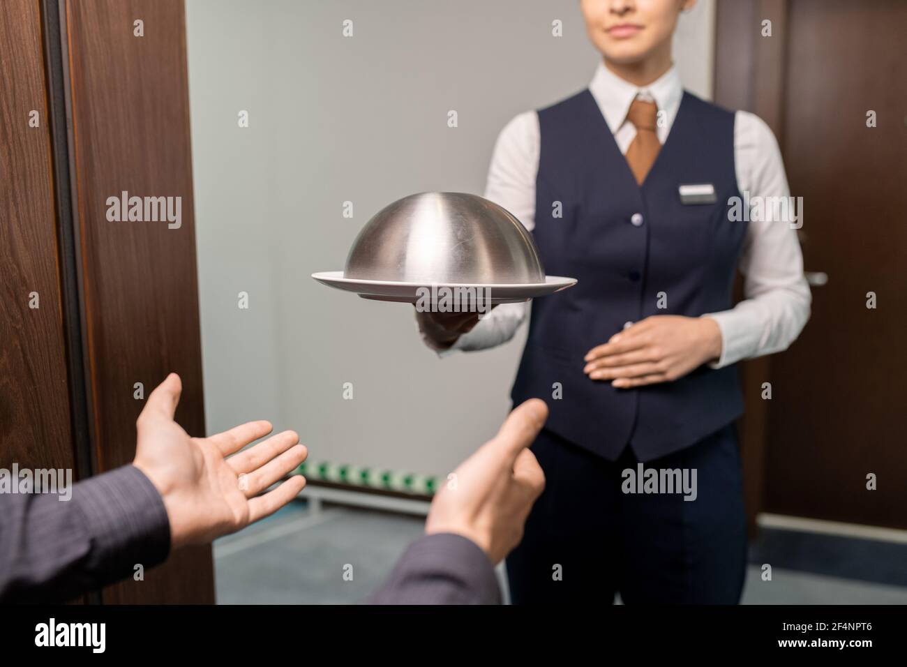 Young elegant female hotel manager passing tray with breakfast to guest ...