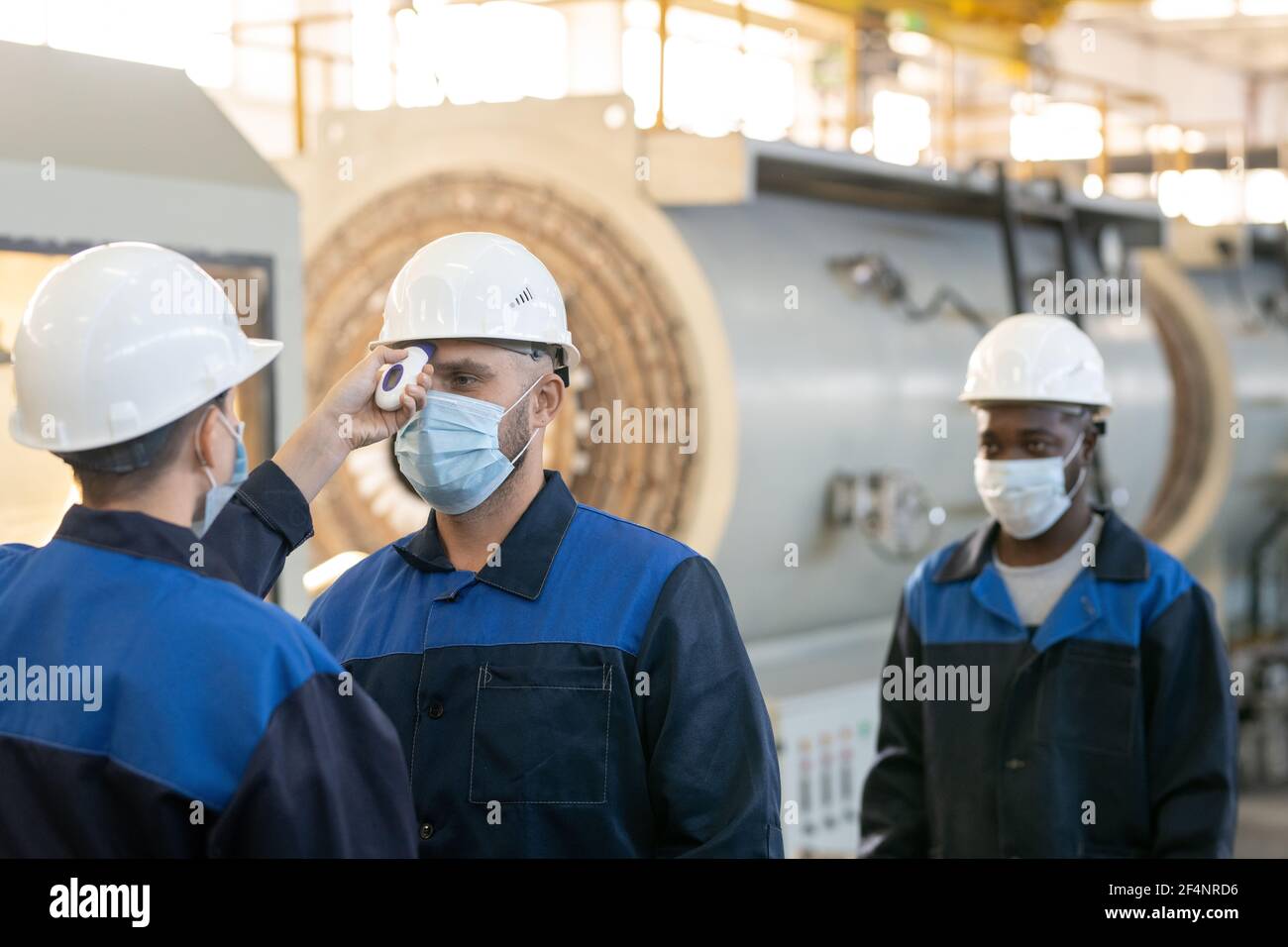 One of several factory workers with thermometer measuring body ...
