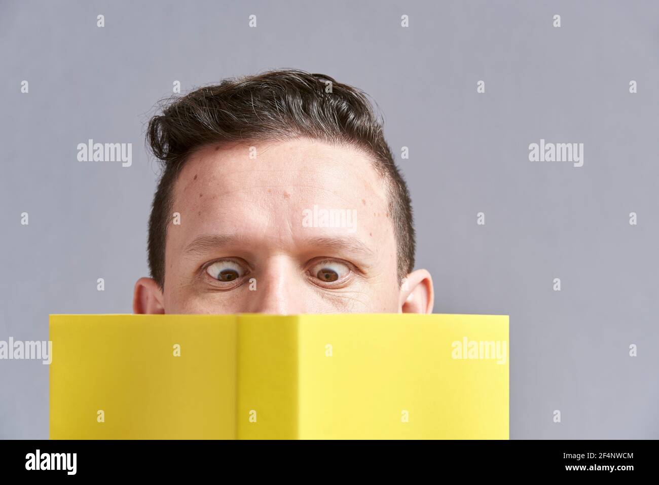Young man reading a yellow book with squinted eyes; a comical, funny ...