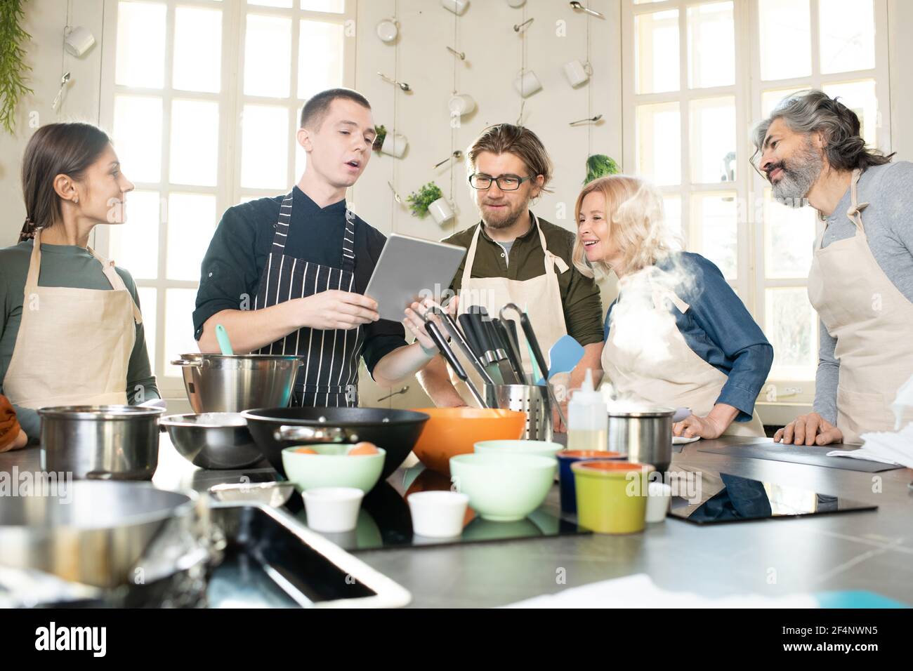 Group of young and mature people in aprons looking at screen of tablet ...