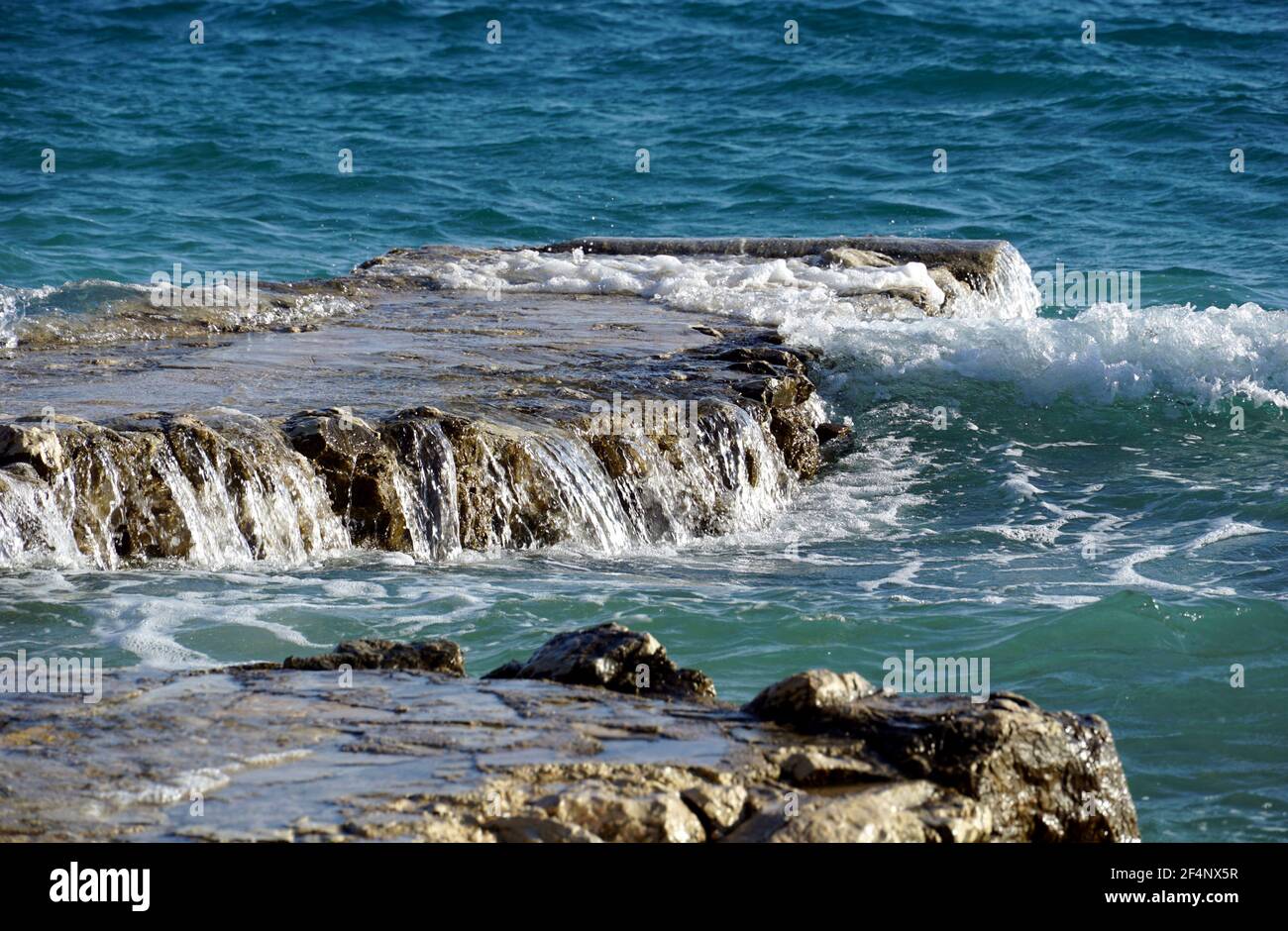Wavy seawater overflowing over a stone reef with deep blue sea in the ...