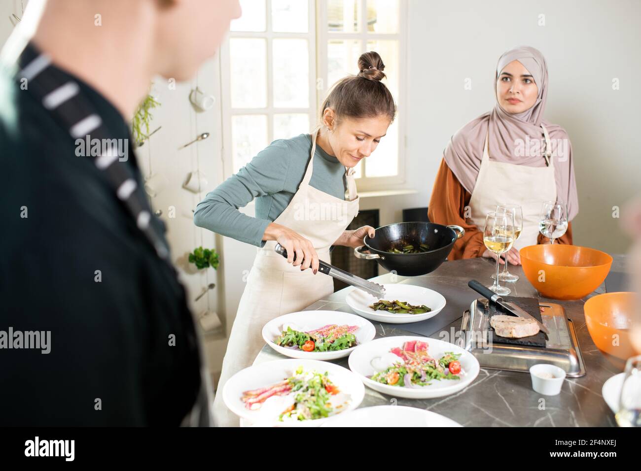 Young pretty blond female with frying pan bending over large kitchen ...
