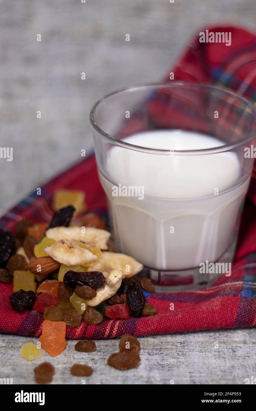 glass of milk near dried fruits, candied fruits, raisins, nuts on plaid ...