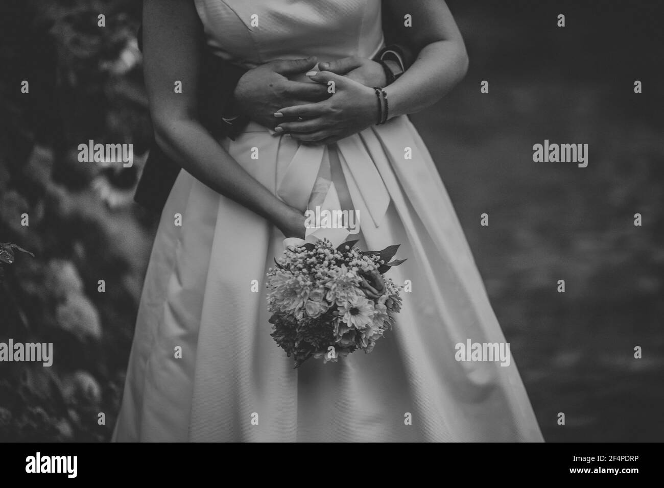Grayscale shot of a newly married couple hugging in a park with a ...