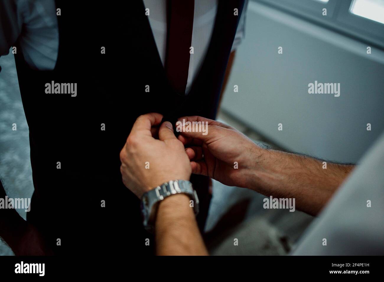 Adult male buttoning the waistcoat of the groom in a dressing room ...