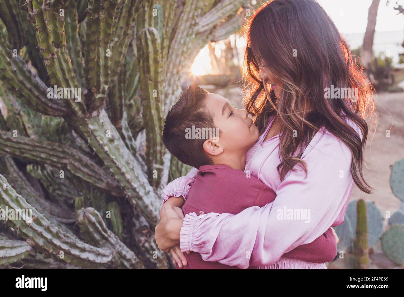 Mother hugging son, both looking at each other with back light sun ...