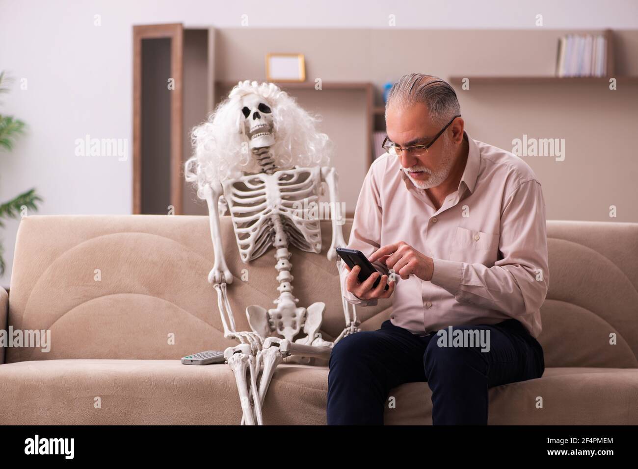 Old man sitting on the sofa with the female skeleton in undying love ...