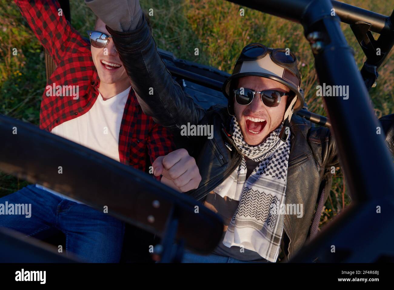 two young happy excited men enjoying beautiful sunny day while driving a off road buggy car ...