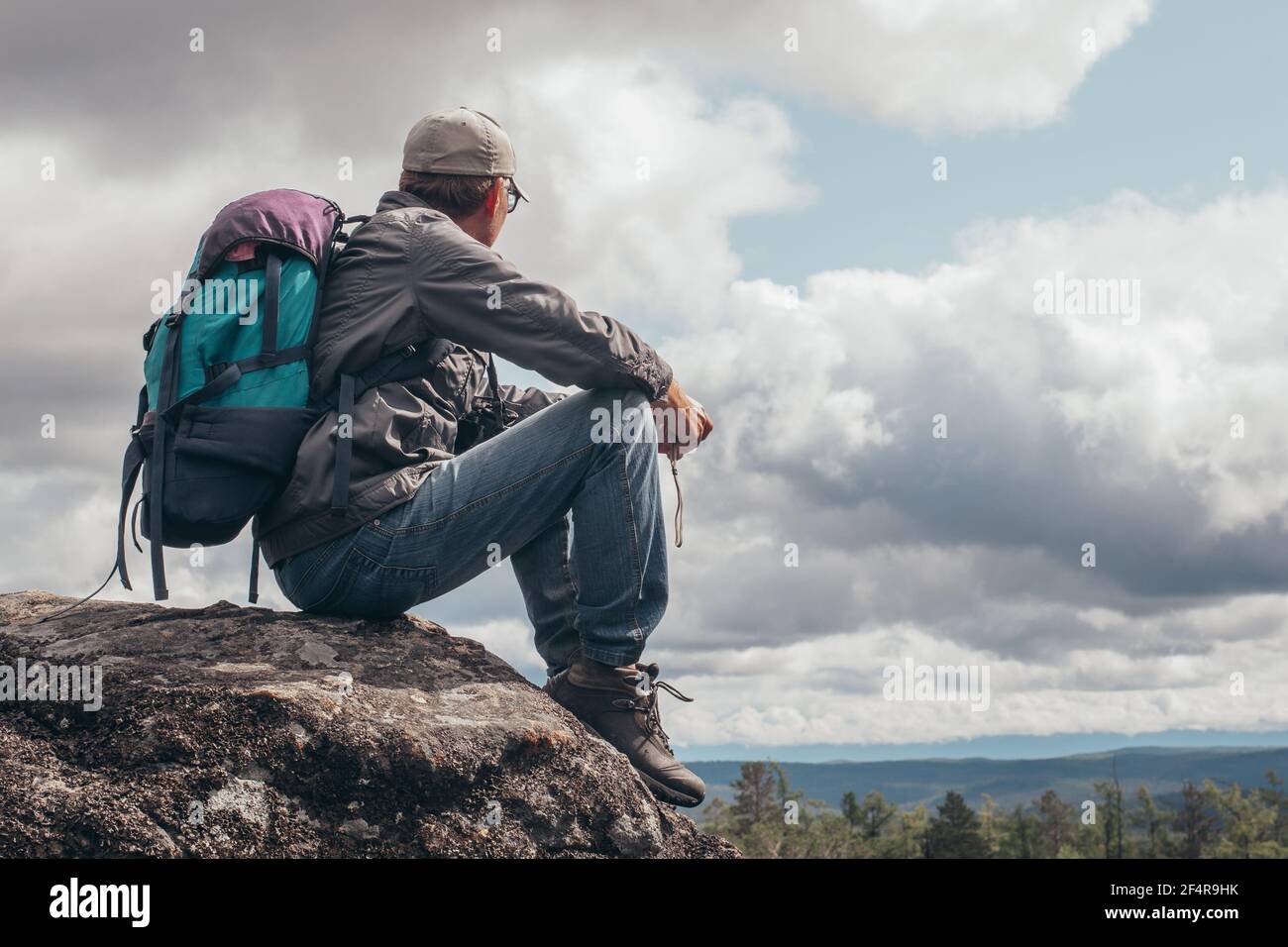 Tourist with backpack sits on the top of the mountain,resting and ...