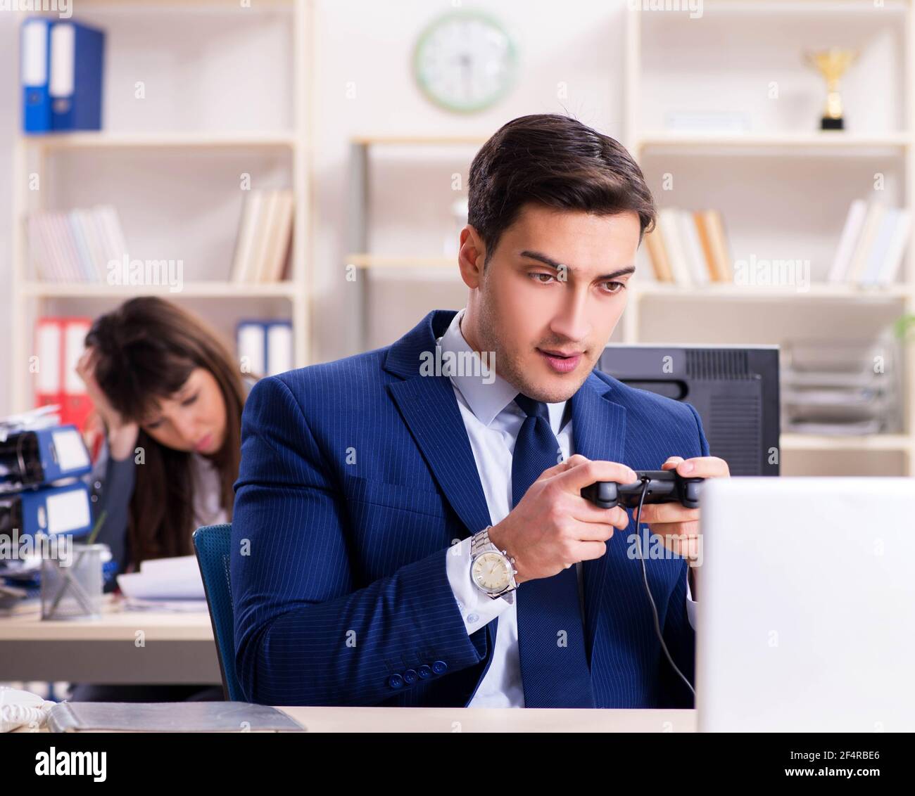 The man playing games in office while colleague is busy Stock Photo - Alamy