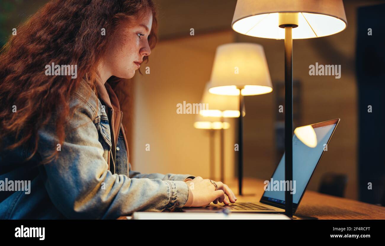 Girl in library at night using laptop. Female student studying on ...