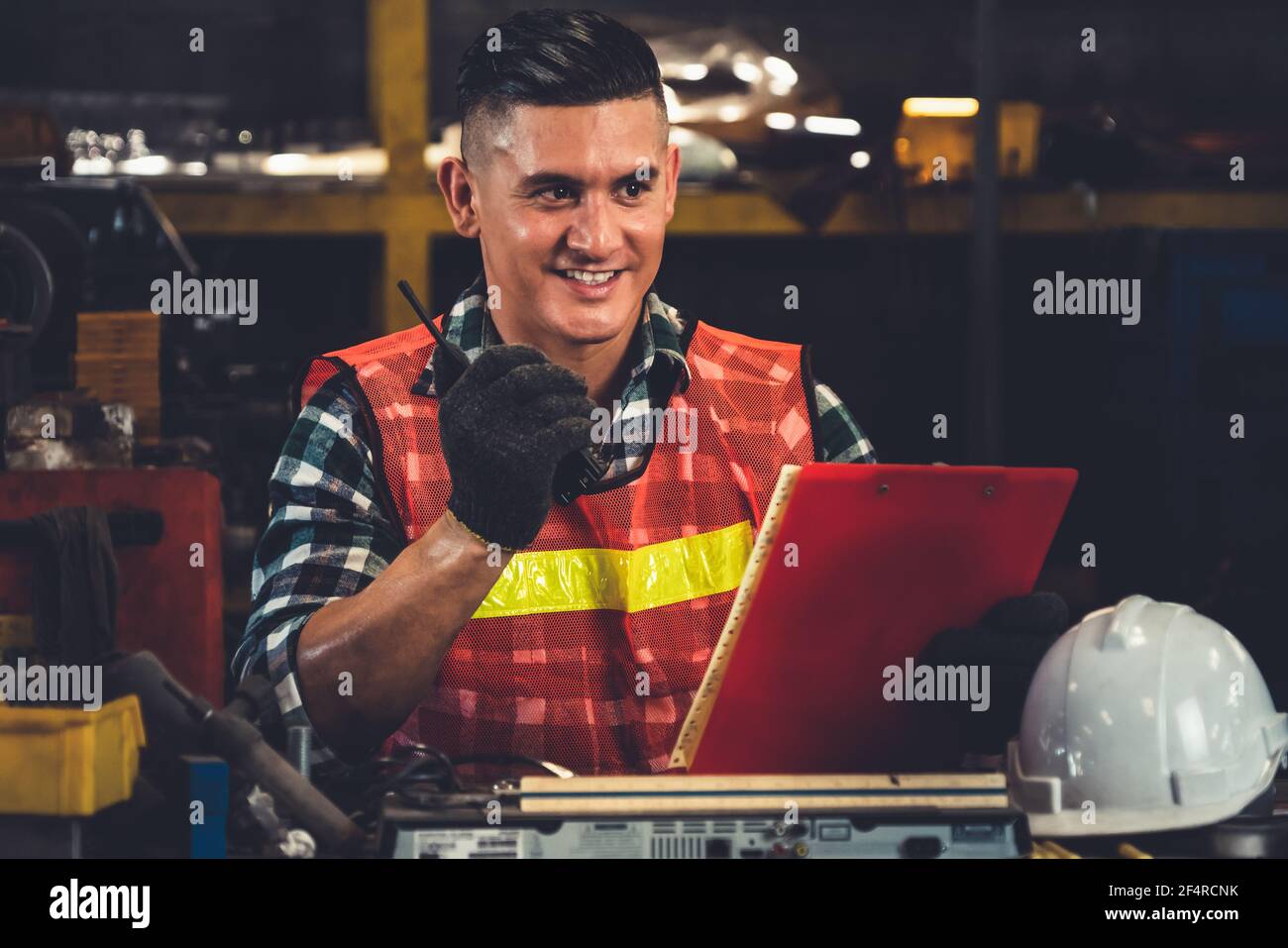 Factory worker talking on portable radio while inspecting machinery ...