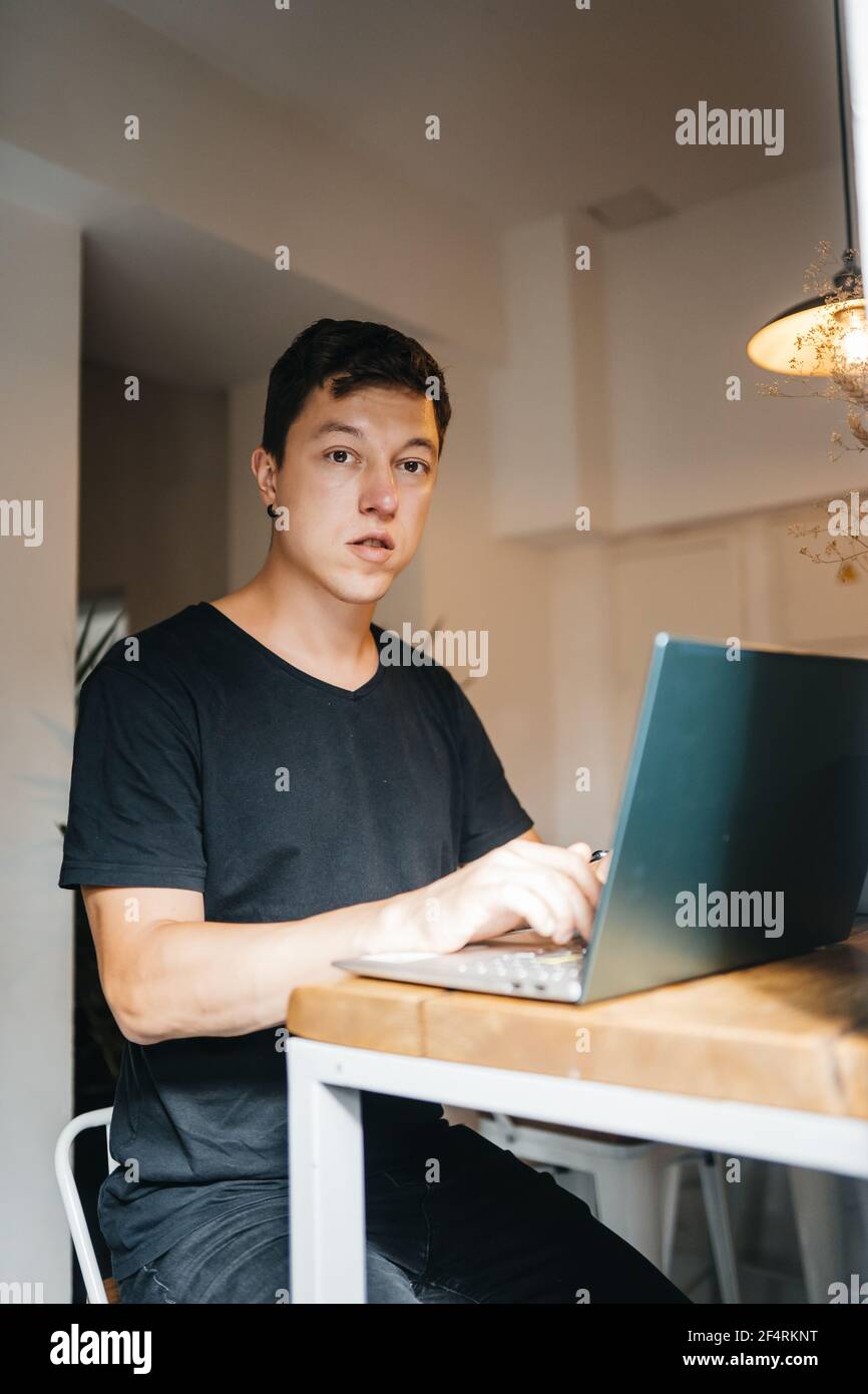 Portrait of man sitting at a table at home working on a laptop computer ...