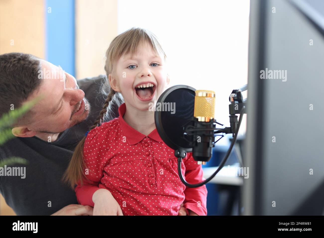 Little girl sitting on her fathers lap and singing song into microphone ...