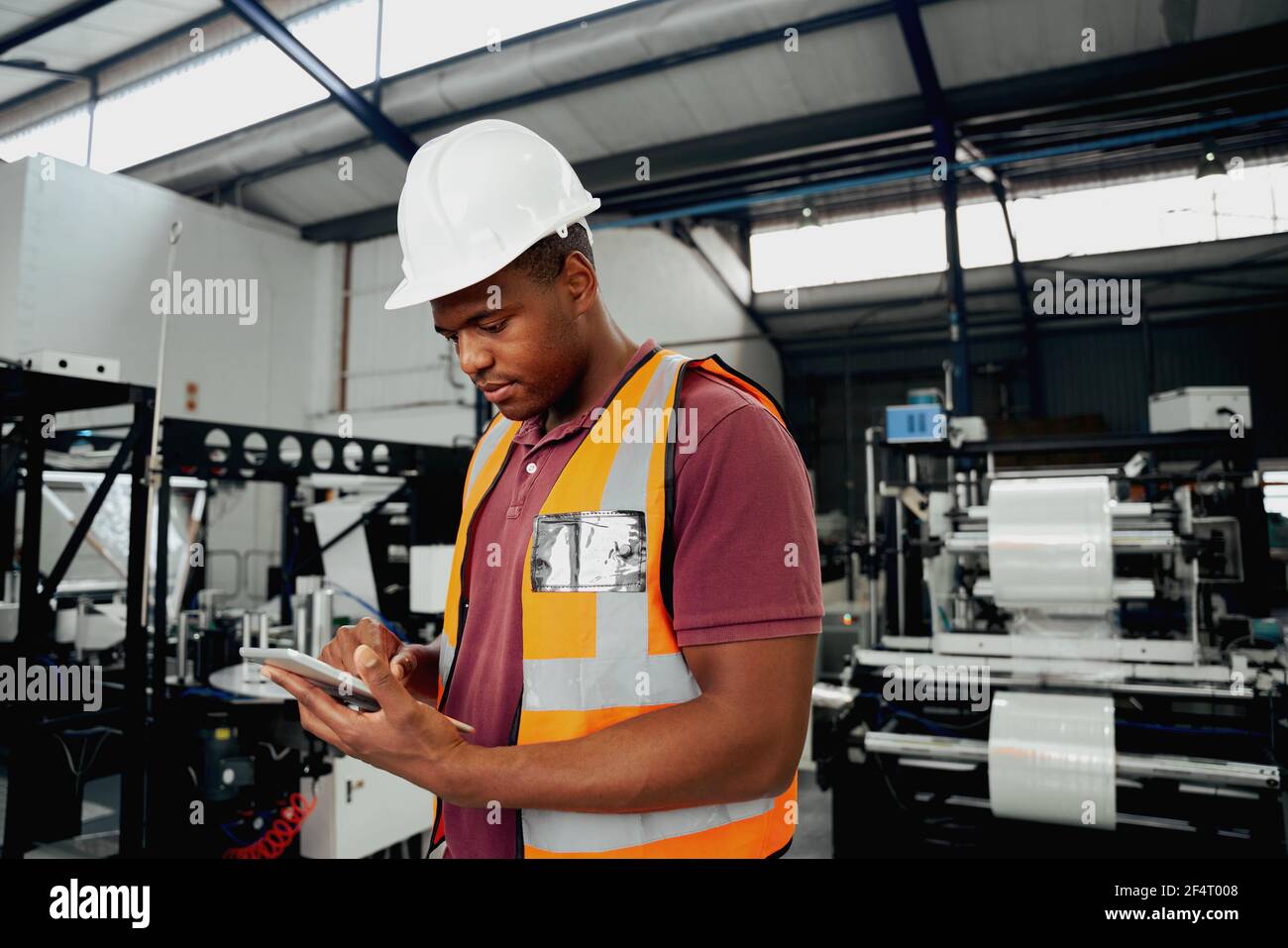 Factory employee checking portable device while examining machinery in ...