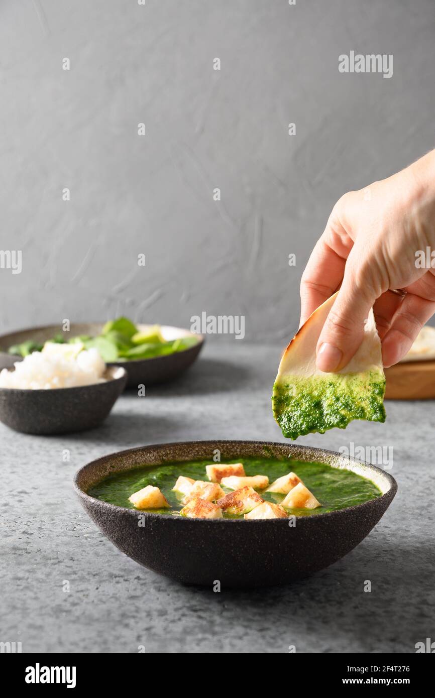 Woman dipped chapati to Palak paneer on grey background. Indian ...