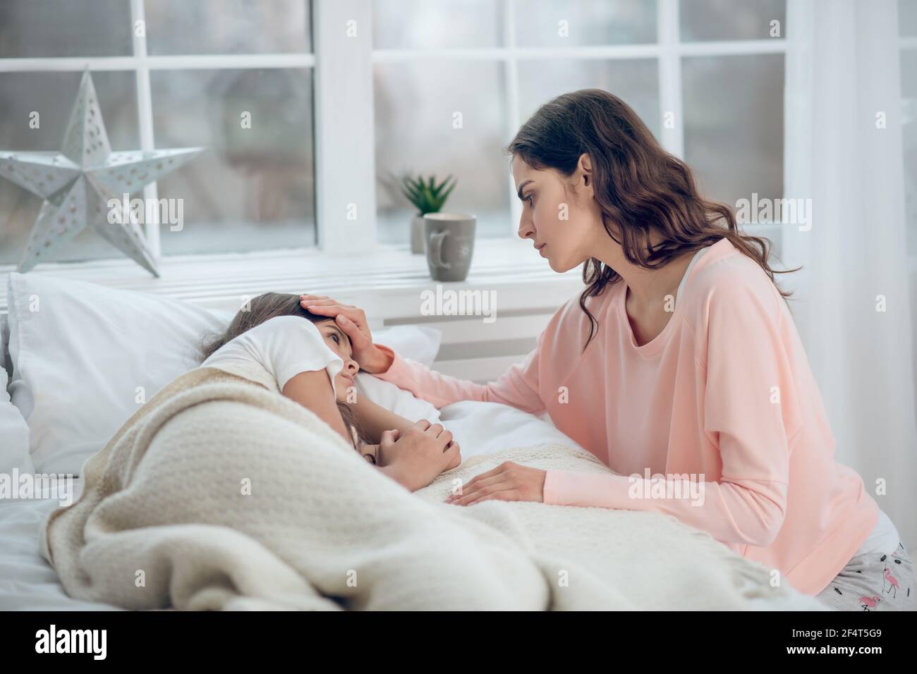 Attentive mother touching forehead of lying sad daughter Stock Photo ...