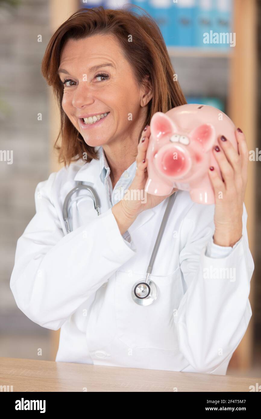 smiling mature doctor woman holding piggy bank Stock Photo - Alamy