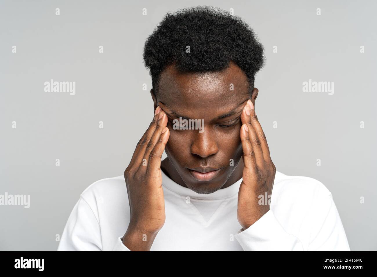 Exhausted upset African American man feeling pain suffering from migraine massaging temples ...