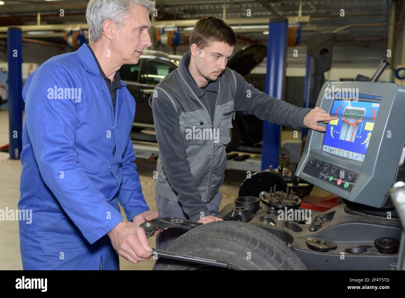 apprentice mechanic and teacher retreading wheel in automotive workshop ...