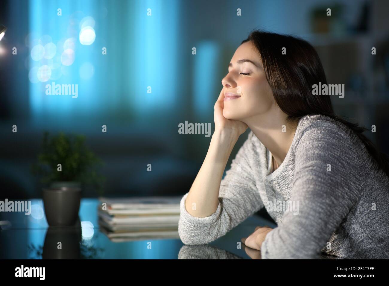 Relaxed woman with closed eyes resting in the living room in the night ...