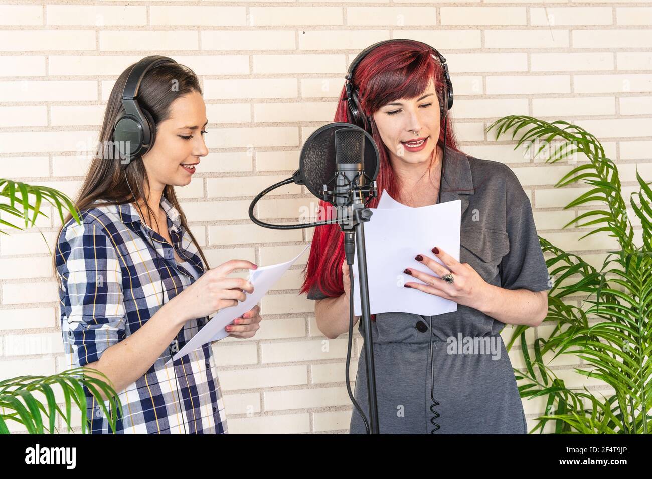 Young women in headphones reading script from papers while standing ...