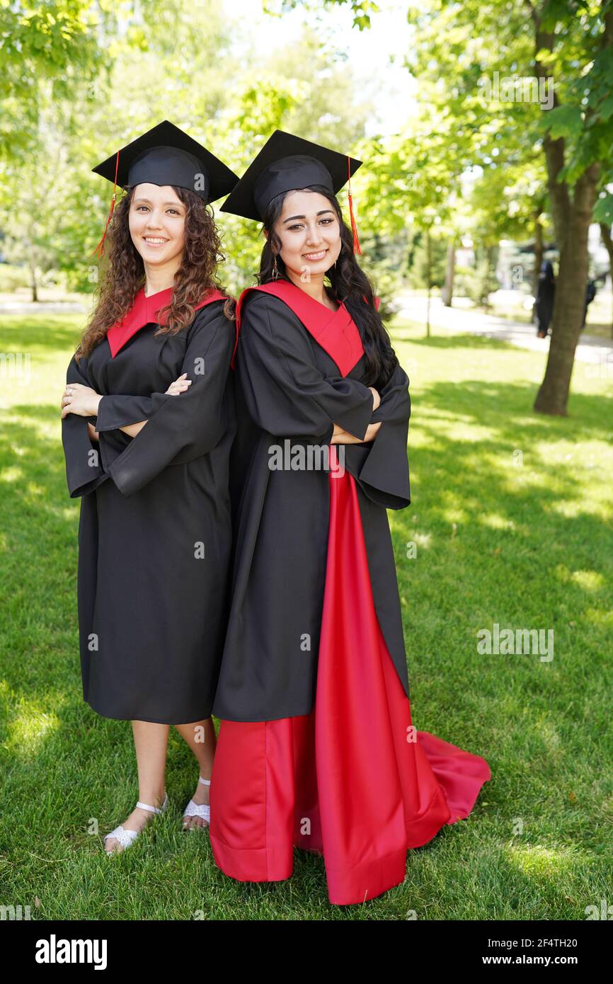 Portrait of successful graduate female students wearing cap outdoors ...