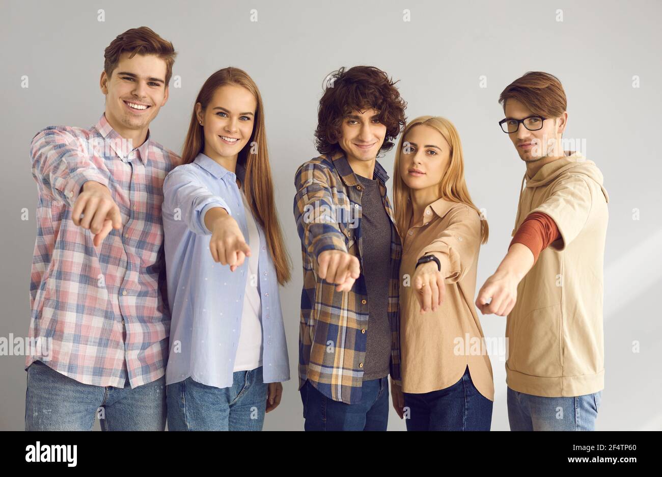 Group of happy young people standing together and pointing at camera ...