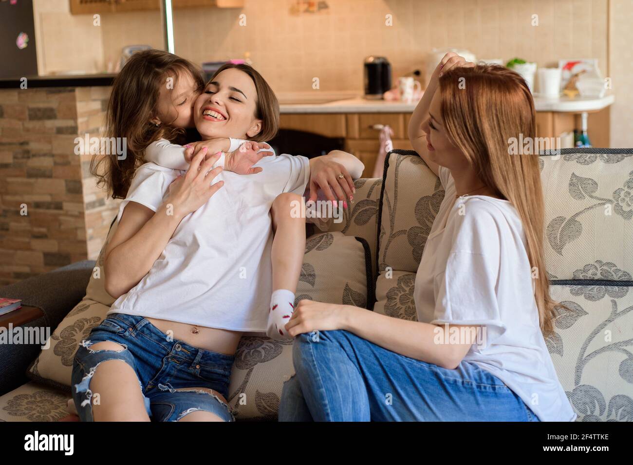 Two sisters and little daughter smiling and hugging at home interior ...