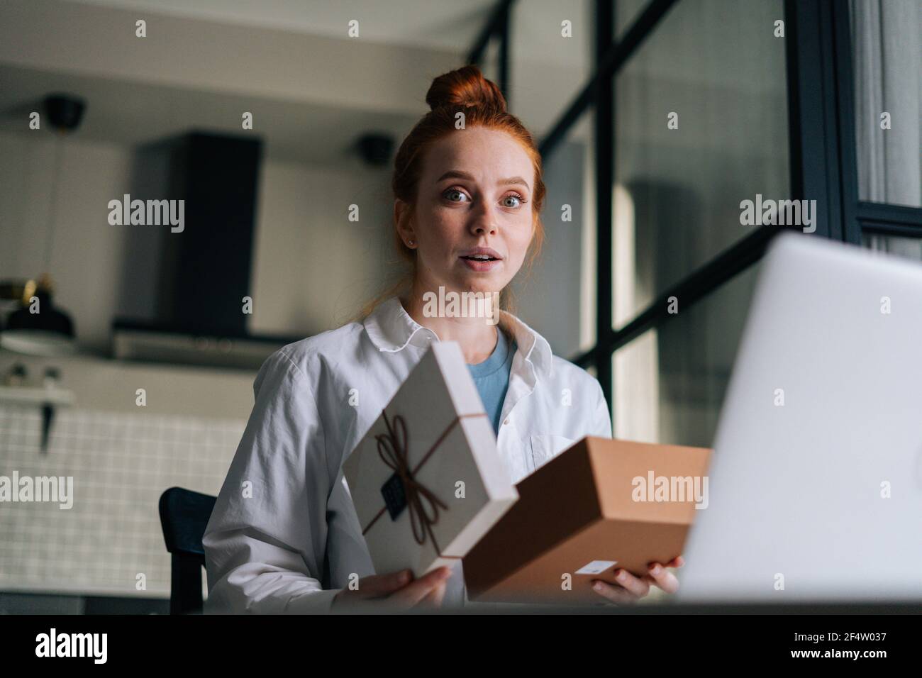 Low-angle shot of shocked redhead young woman opening gift box with ...