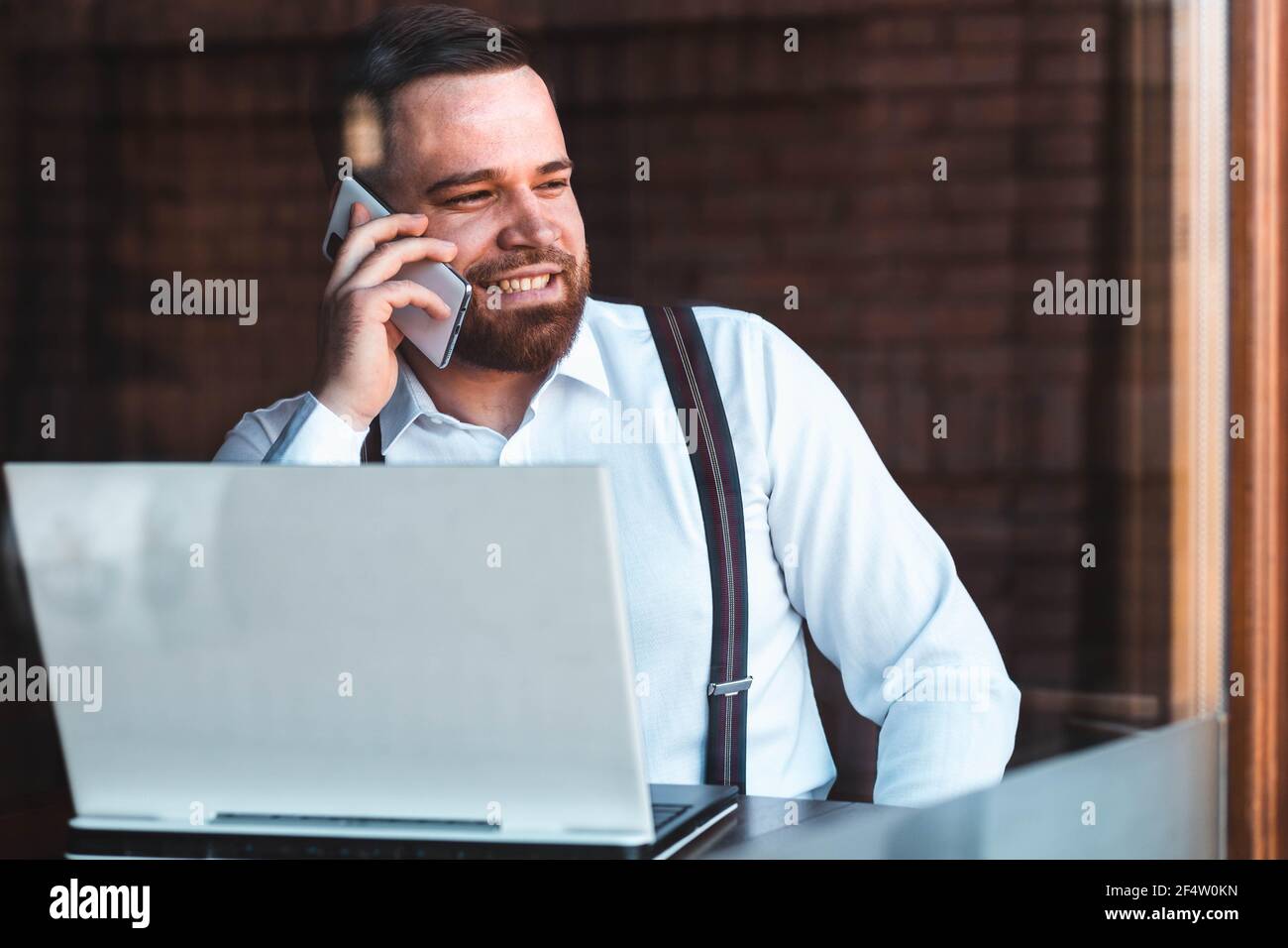 Young hipster, businessman talking over a phone in a cafe, laptop on ...