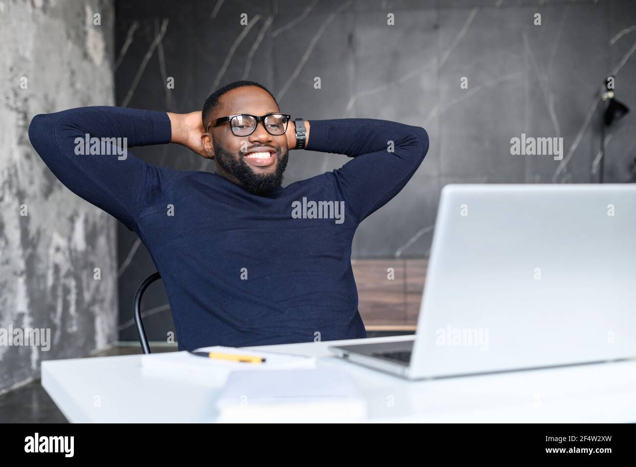 Relaxed African-American male entrepreneur leaned back in chair, holds ...