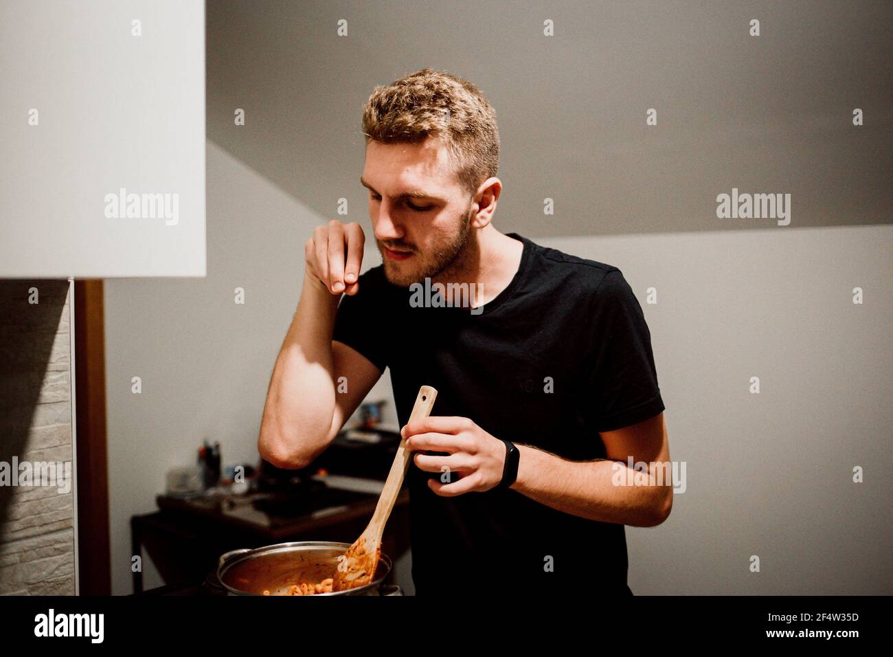 Young man in the kitchen adding salt to a delicious meal before tasting ...