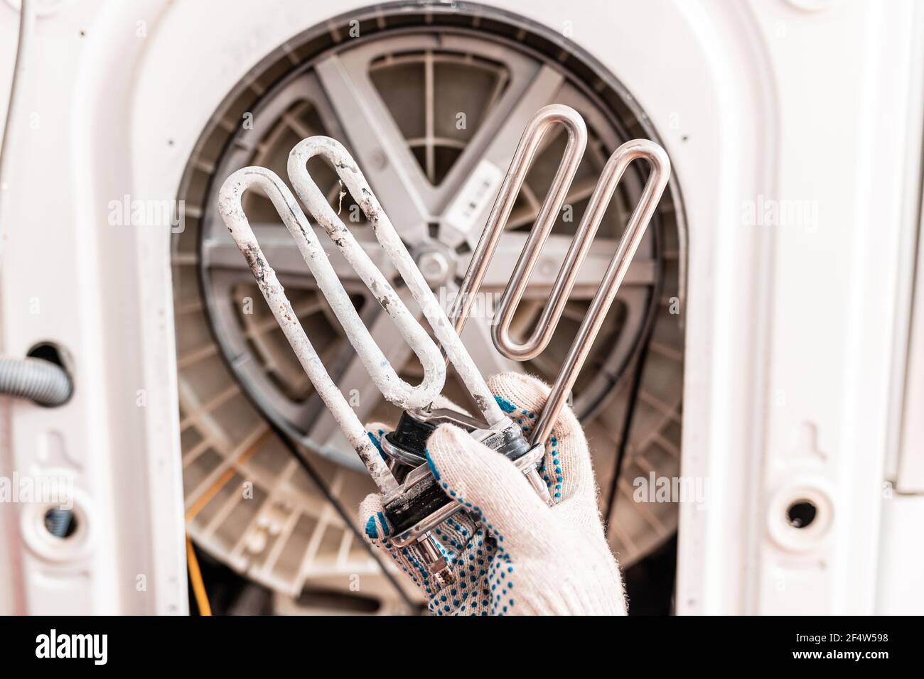 A worker holds a broken and new washing machine heating element. Close ...