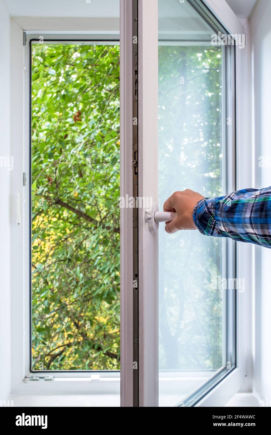 Man hand opens a PVC window from which you can see a tree in an ...