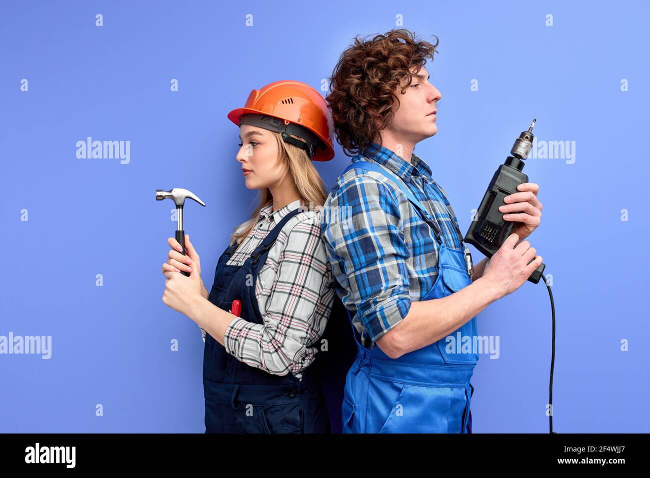 two builders stand back to back to each other holding household tools ...