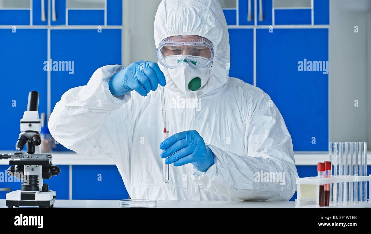 scientist in hazmat suit holding test tube and dropper while working ...