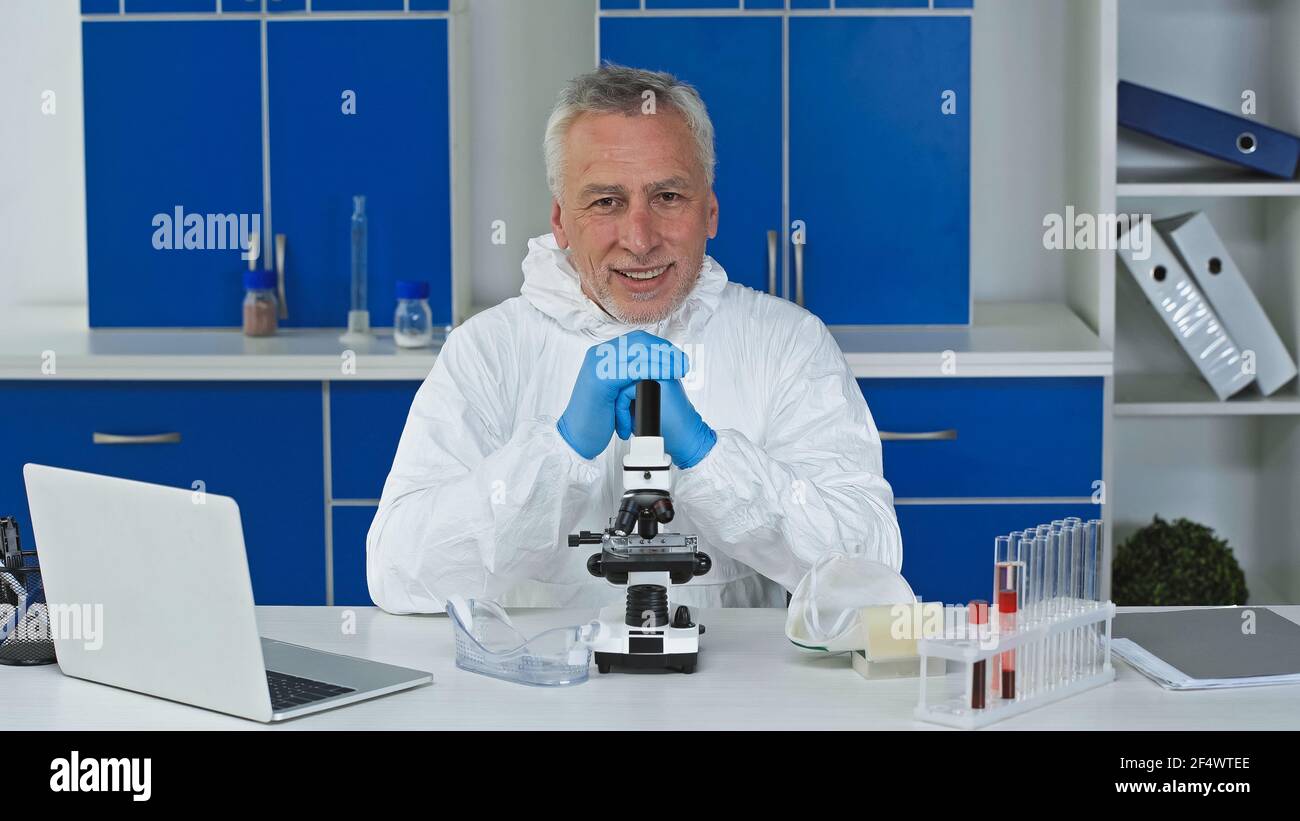smiling scientist in hazmat suit looking at camera near microscope and ...