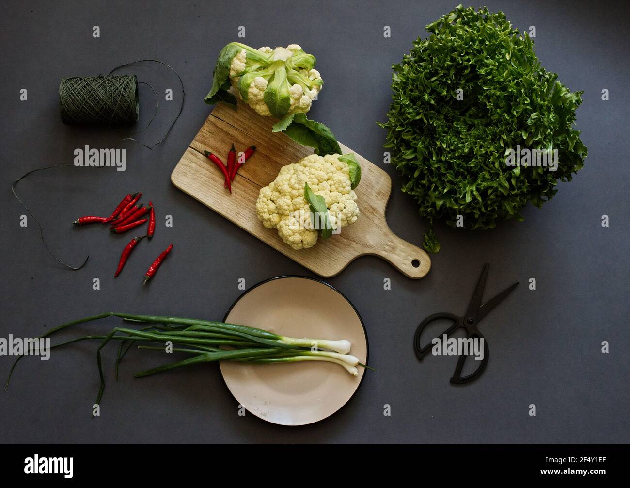 Top view of cauliflowers, chili peppers on a board, scallions, boxwood ...