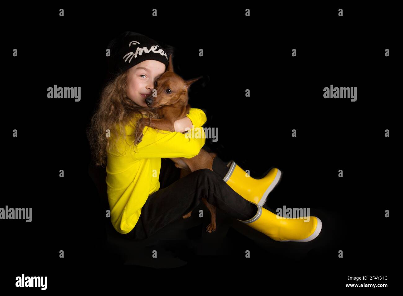 A cute little toddler girl hugs her dog, the Miniature Pinscher. Studio ...