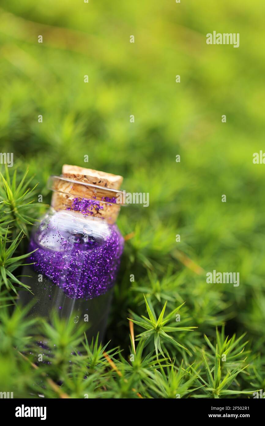 Magic Potion.Bottle with purple shiny glittering liquid in green moss ...