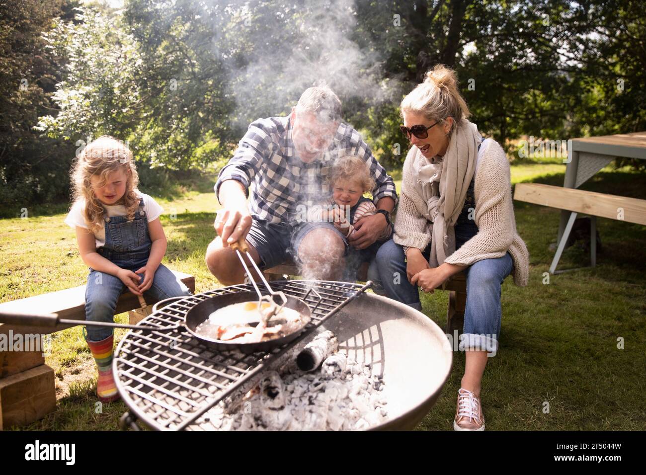 Happy family cooking breakfast on campsite grill Stock Photo - Alamy