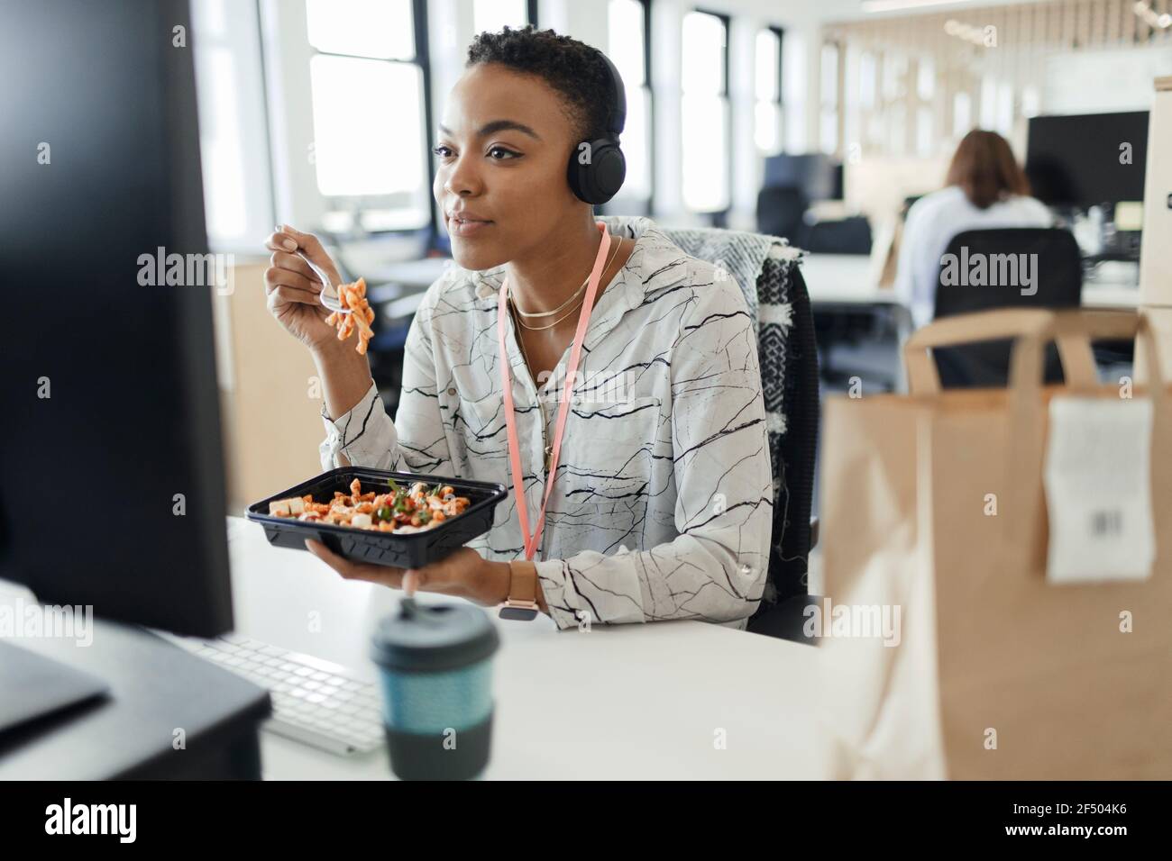 Businesswoman eating takeout lunch at computer in office Stock Photo ...